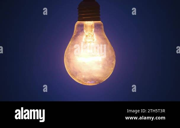 Incandescent lamp lights up and flickers on dark blue background ...
