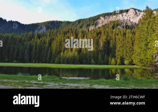 A gleaming wide clear lake reflects bright warm sunlight, against a ...