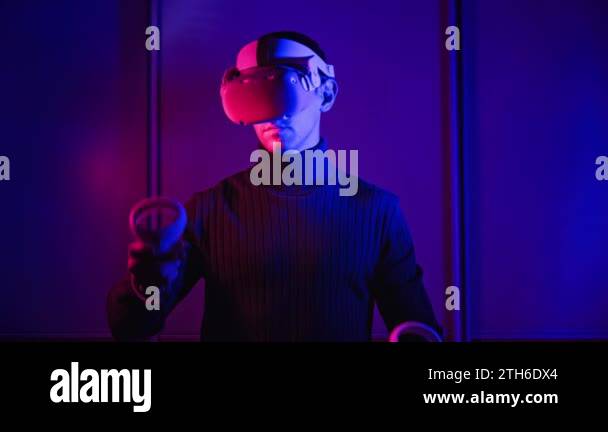 Young man in VR helmet interacts with virtual reality using controllers ...