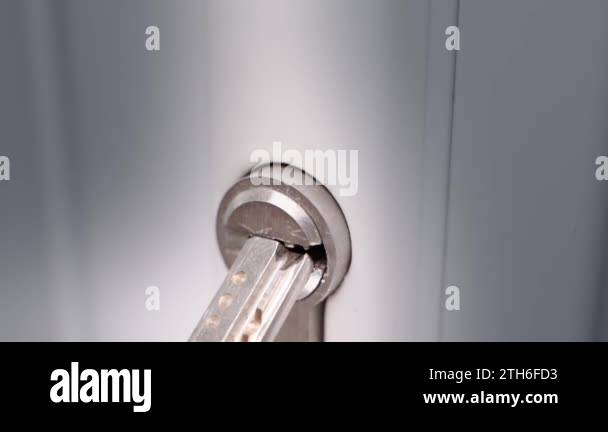 Inserting a key into the keyhole of a white plastic door close-up ...