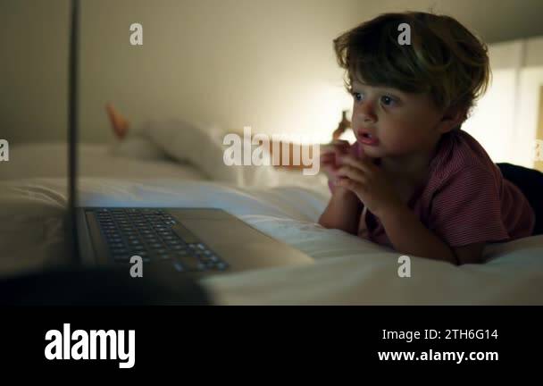 Child watching entertainment media on laptop screen laying in bed at ...