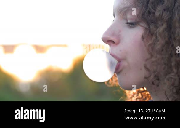 Curly-haired teenage girl inflates a big gum bubble until it bursts. 4K ...