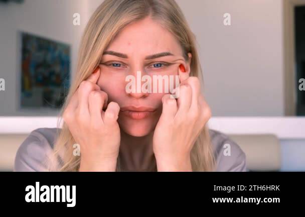 Ageing. Sagging skin. Young woman does facelift exercises by looking in ...