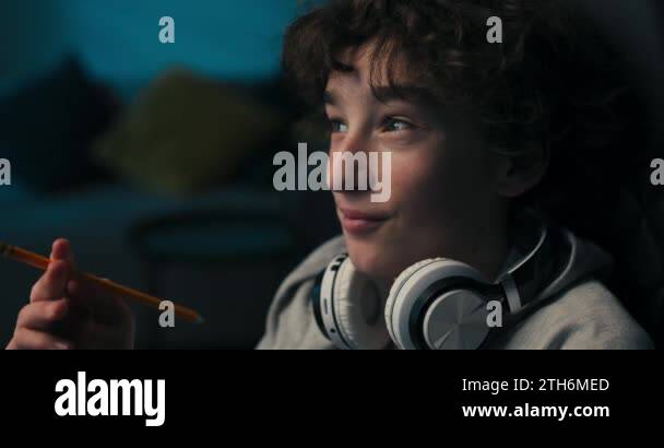 A boy sits in room in the evening in front of computer screen and ...