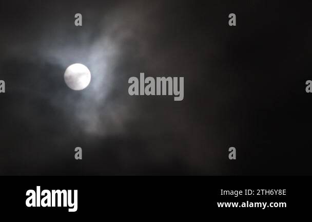 Night sky is illuminated by full moon shining through dark clouds which ...