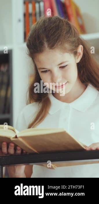 Vertical Screen: Smiling child standing with book by bookshelves and ...