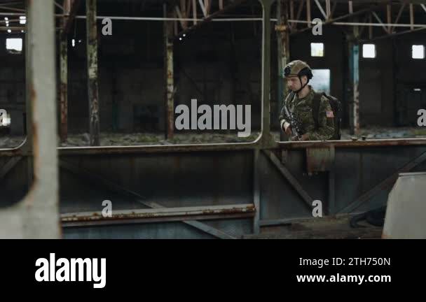 Serious military man with weapon walking alone among captured building ...