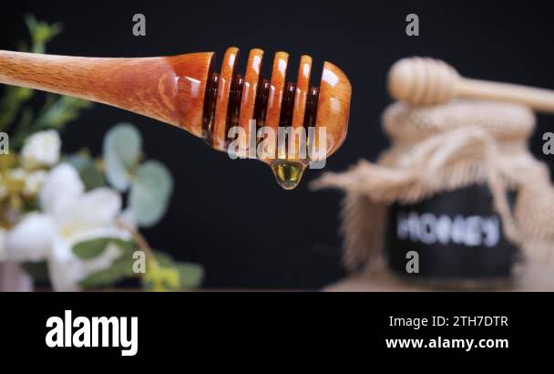 Drop of honey dripping from the spoon on black background in slow ...