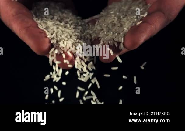 From mens palms pours raw rice. On a black background. Filmed on a high ...