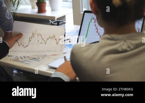 Young coworkers comparing sales result graph on paper with chart on ...