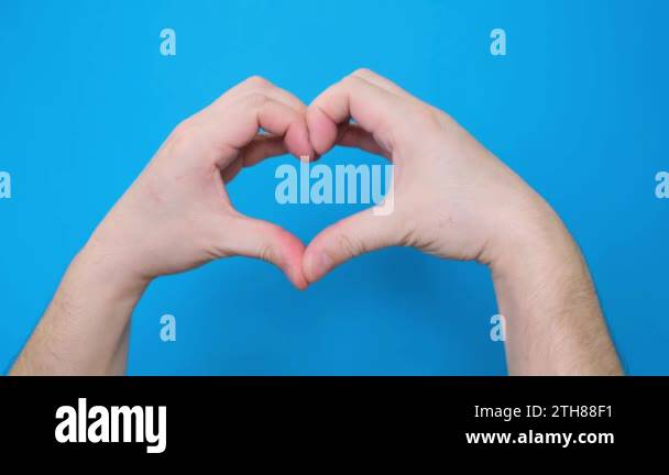 A view of a male hand making a heart-shaped gesture, isolated on a blue ...