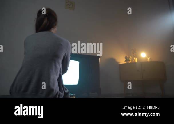 Back view of woman sitting on the ground in old room with dim lighting ...