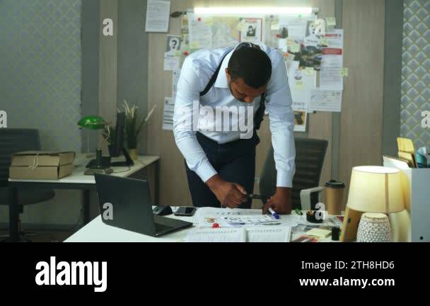 Handsome detective standing over the table examines files with a ...