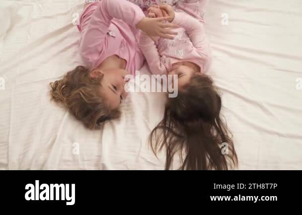 Little girls in pink pajamas laying on the bed upside down, smiling and hugging each other Stock ...