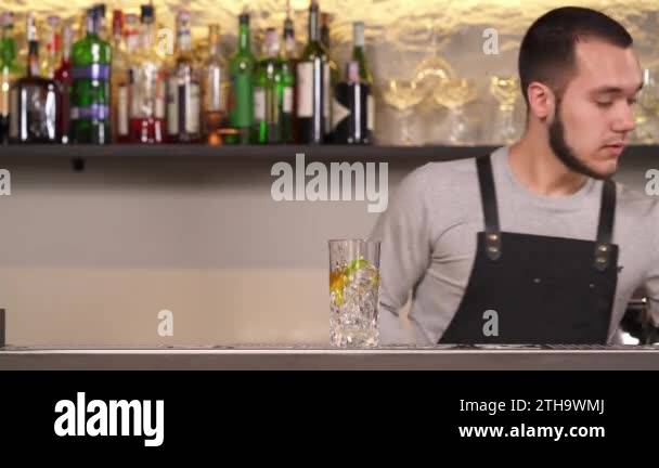 Bartender pours a sparkling water from the soda siphon to the glass filled with ice cubes ...