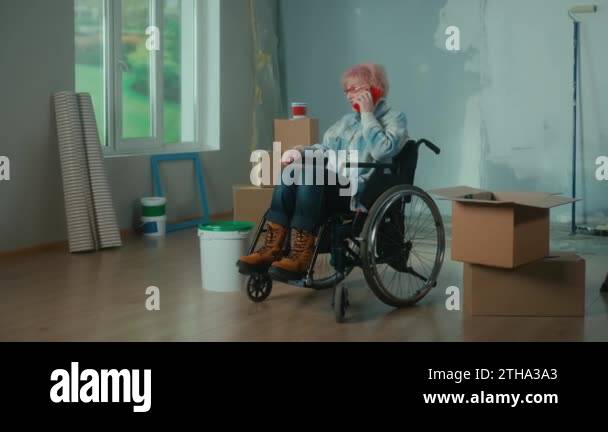 An elderly disabled woman moves in a wheelchair and talks on a mobile ...