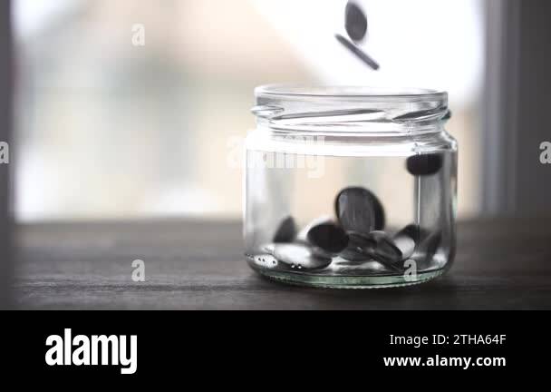 Ukrainian coins falling into the glass jar on wooden table near window ...