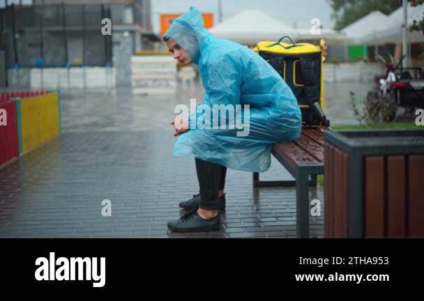 Wide shot side view of sad young courier sitting on rainy day in city ...