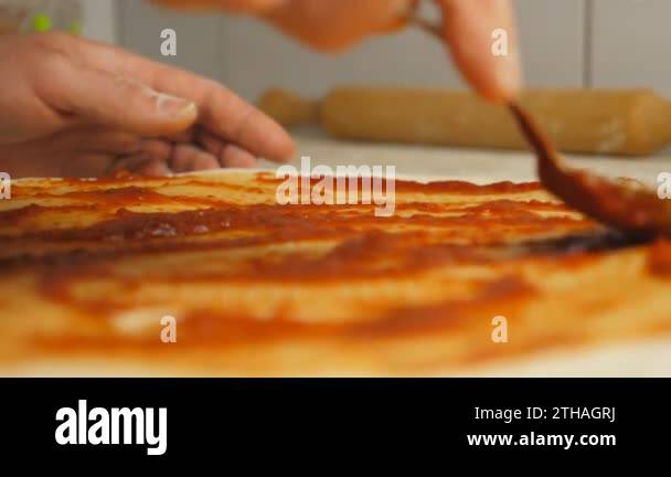 Male arm of cook applying ketchup on pizza dough using a spoon at ...