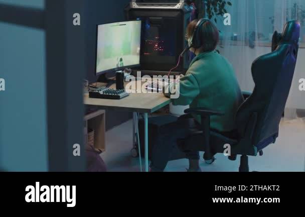 Full side shot of female gamer sitting in room at night, playing first ...