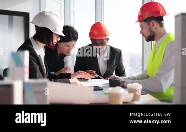 Group of four multiracial people architects sitting at desk with lots ...