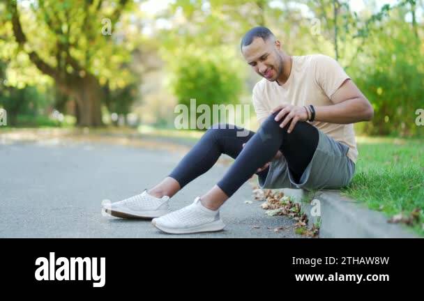 Young athlete runner sitting with muscle pain in city park. Man ...