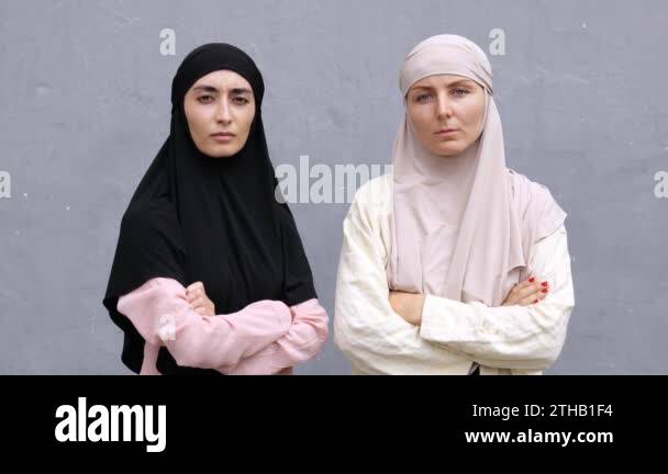 Two serious frowning Muslim women in chimaras stand with their arms ...