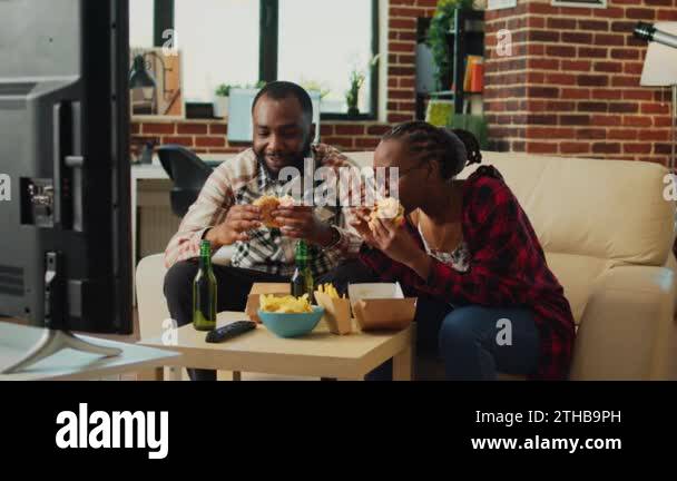 Modern life partners taking bite of cheeseburger, eating fast food from ...