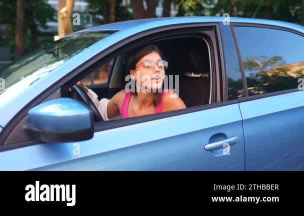 A young angry woman peeks out of the car window. A woman shows her ...
