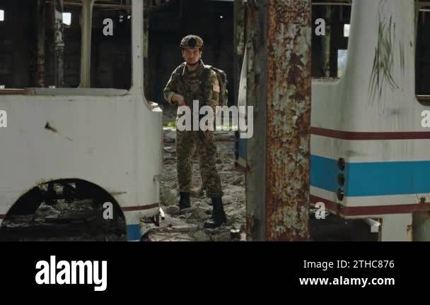 Concentrated soldier with sniper rifle standing between destroyed buses ...