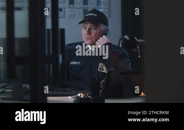 Security officer sits by table and looks view from security cameras ...