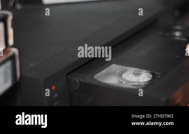 Male hand inserts VHS cassette into a VCR Video recorder. Black vintage ...