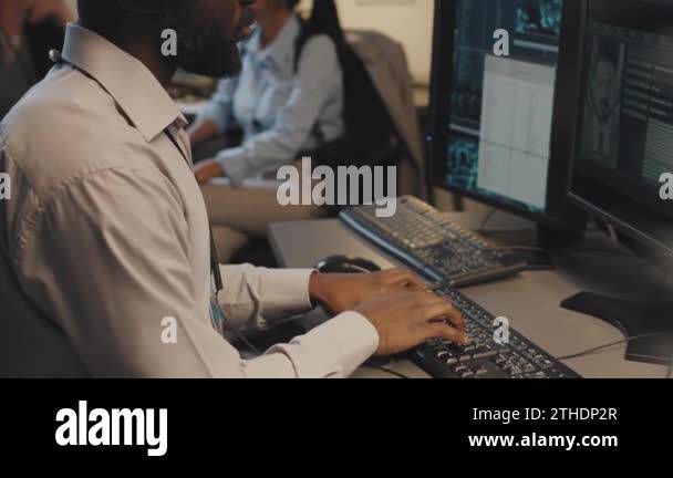 Side view tilting up of young Black man using computer, searching FBI criminal database, two ...