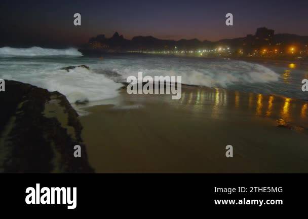 Slow motion, pan right of waves crashing against the sand and surfers ...