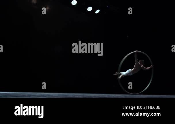 Muscular circus artist perform Cyr Wheel on a black background stage ...