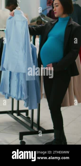 Vertical video: Asian woman with baby bump shopping for clothes in ...