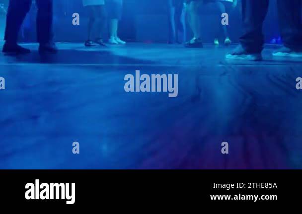 Low angle floor level view of the feet of people dancing in moody blue ...