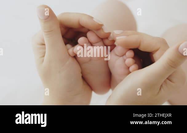 Caring mom holds baby feet in her hands forming a heart shape. Tiny ...