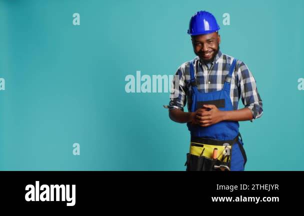 Young male contractor standing over blue background, wearing building ...