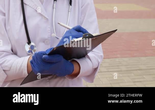 Young female nurse standing outside hospital infirmary writing patient ...