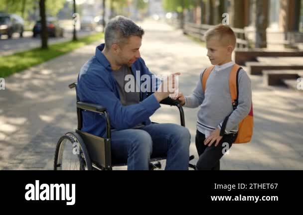 Disabled father tells his son a story and fixing his backpack after ...