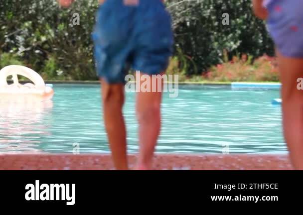 Two young boy running and jumping into swimming pool water in slow ...