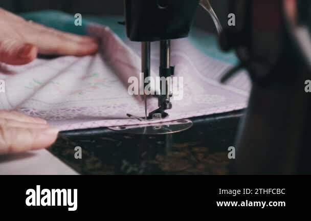An aged seamstress sews at a traditional sewing machine at home in slow ...