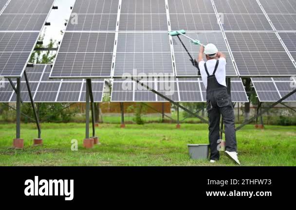 Worker cleaning solar photovoltaic panels by mop. Back view of man ...