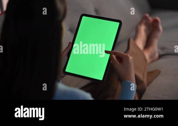 Rear view of young woman relaxing on couch, scrolling at green screen ...