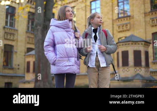 Two sad Caucasian teen schoolgirls standing on schoolyard talking with ...