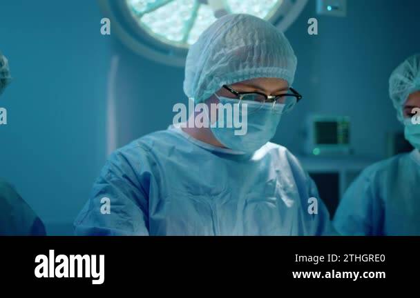 A surgeon and his two assistants are wearing surgical gear and ...