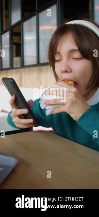Teenage girl absorbed in smartphone screen while eating fast food ...