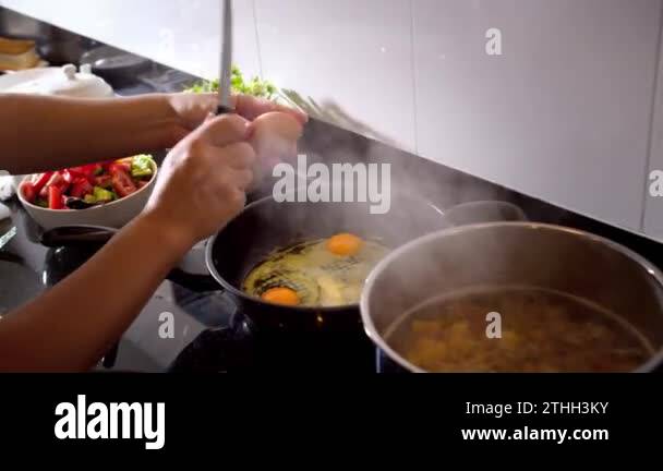 Cooking scrambled eggs in a pan. Woman breaks eggs in a frying pan to ...