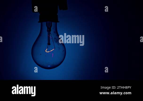 Light bulb lights up on a blue background in the dark. Slow turning on ...